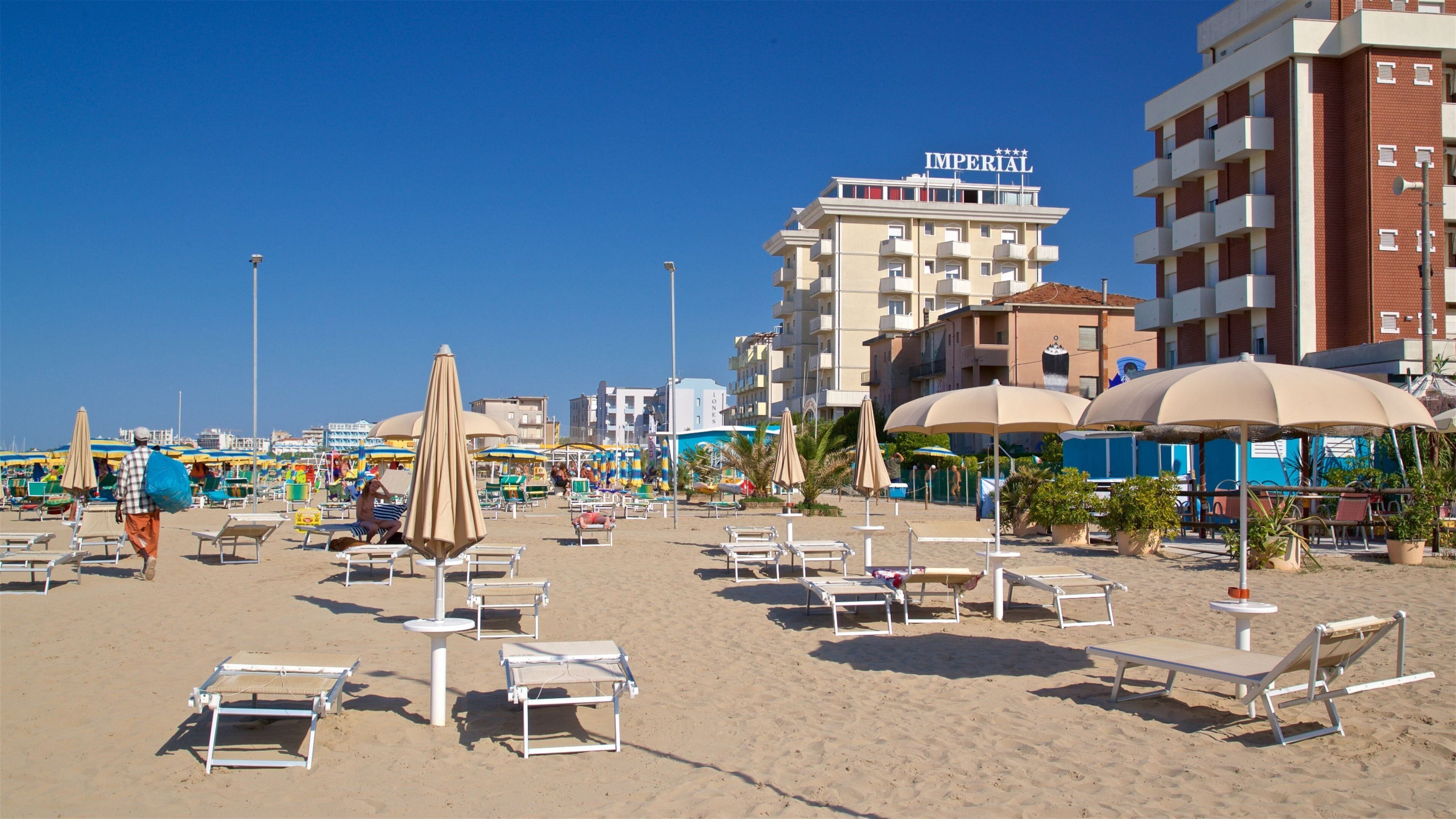 Uma praia com espreguiçadeiras, guarda-sóis e um edifício com a placa 'IMPERIAL'.