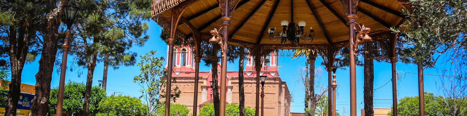 Um coreto com detalhes metálicos elaborados e um edifício vermelho ao fundo.