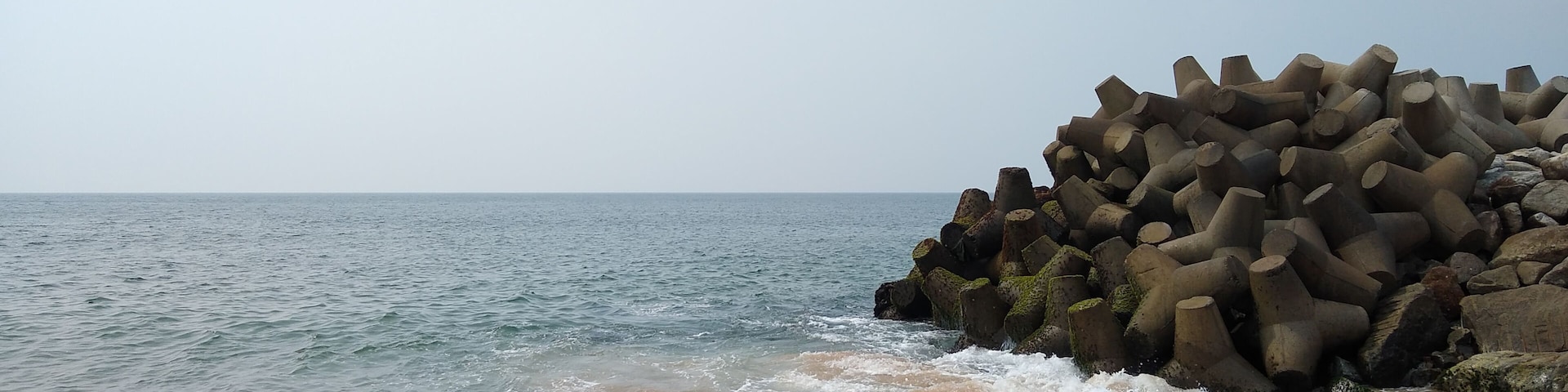 Uma praia com ondas quebrando na costa e um monte de estruturas cilíndricas de concreto.