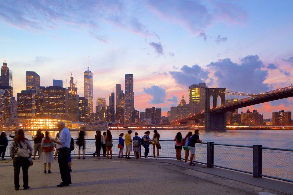 Horizonte urbano com edifícios iluminados e uma ponte ao entardecer.