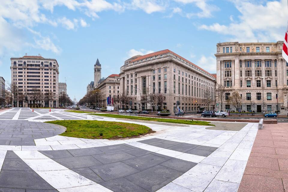 Uma praça urbana com uma grande área central, edifícios históricos e bandeiras.