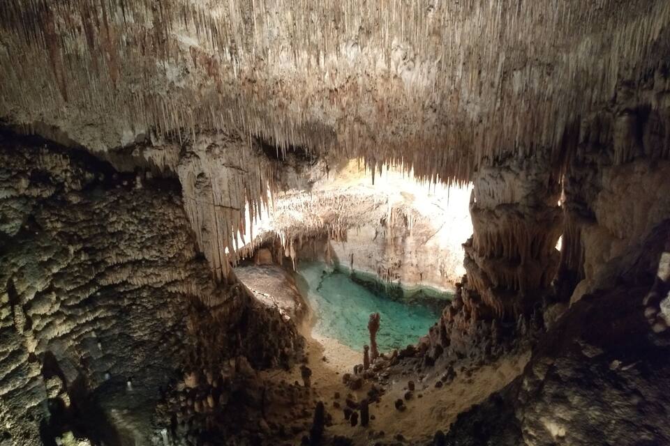 Caverna com estalactites penduradas no teto e um lago no fundo.