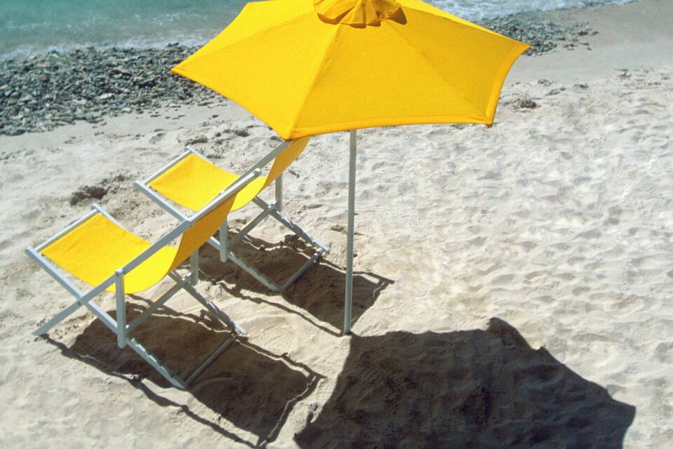 Uma praia com um guarda-sol amarelo e duas cadeiras de praia amarelas.