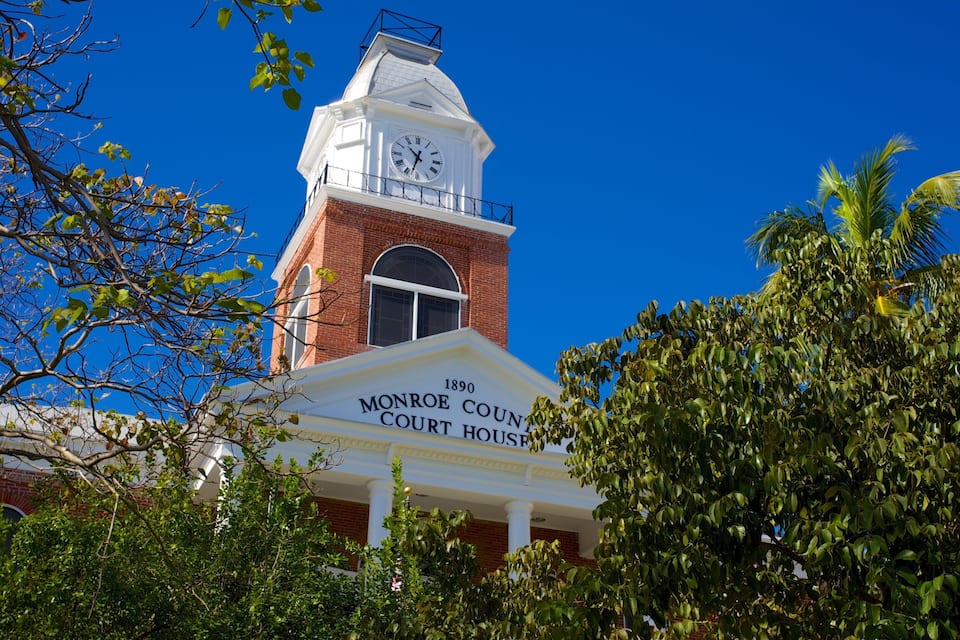 O Tribunal do Condado de Monroe com uma torre do relógio, rodeado por árvores e um céu azul límpido.