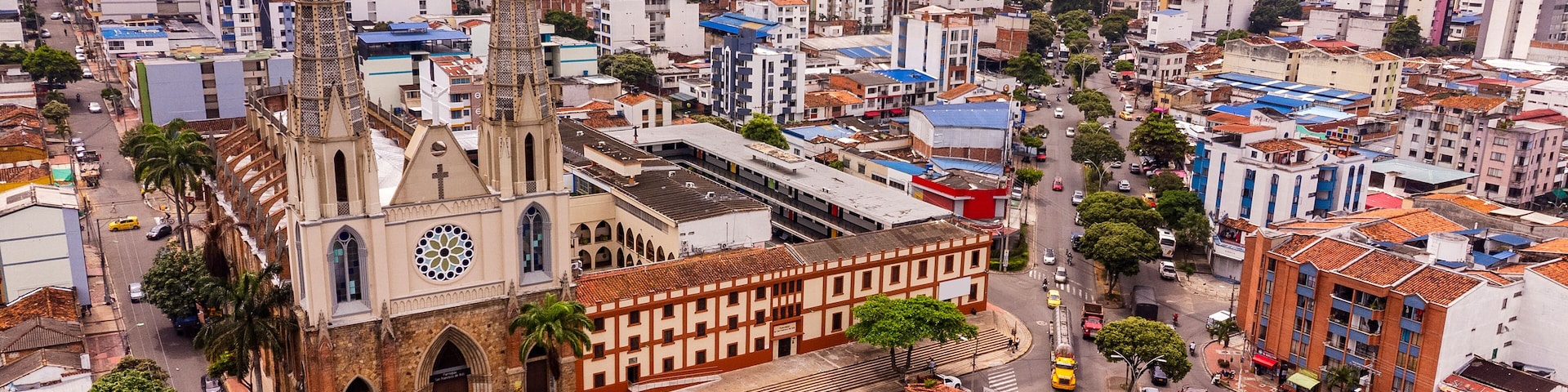 Paisagem urbana com uma igreja imponente, destacando-se por um grande relógio e duas torres, cercada por edifícios e ruas movimentadas.