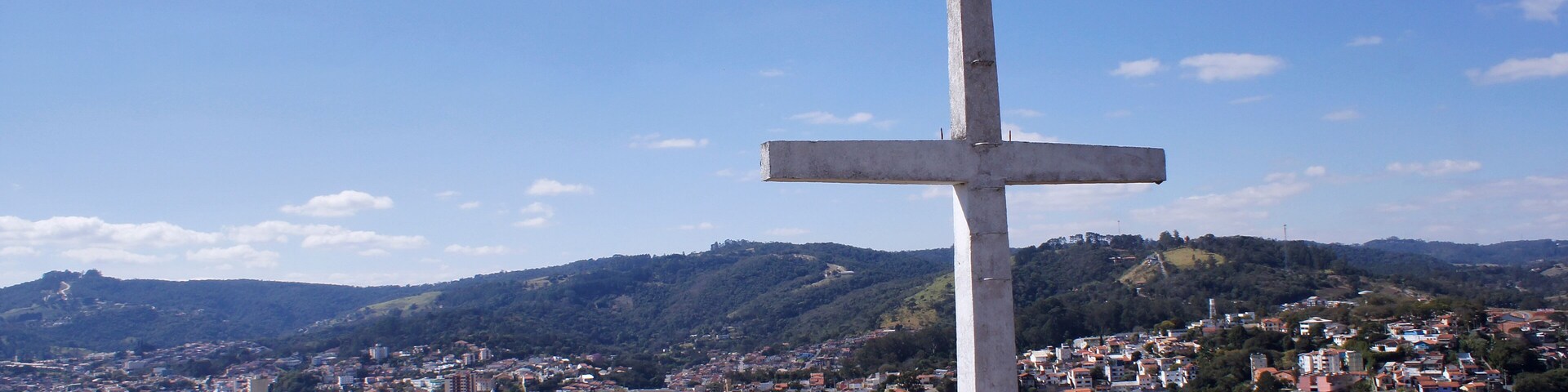 Um monumento em forma de cruz com vista para uma paisagem urbana e colinas ao fundo.