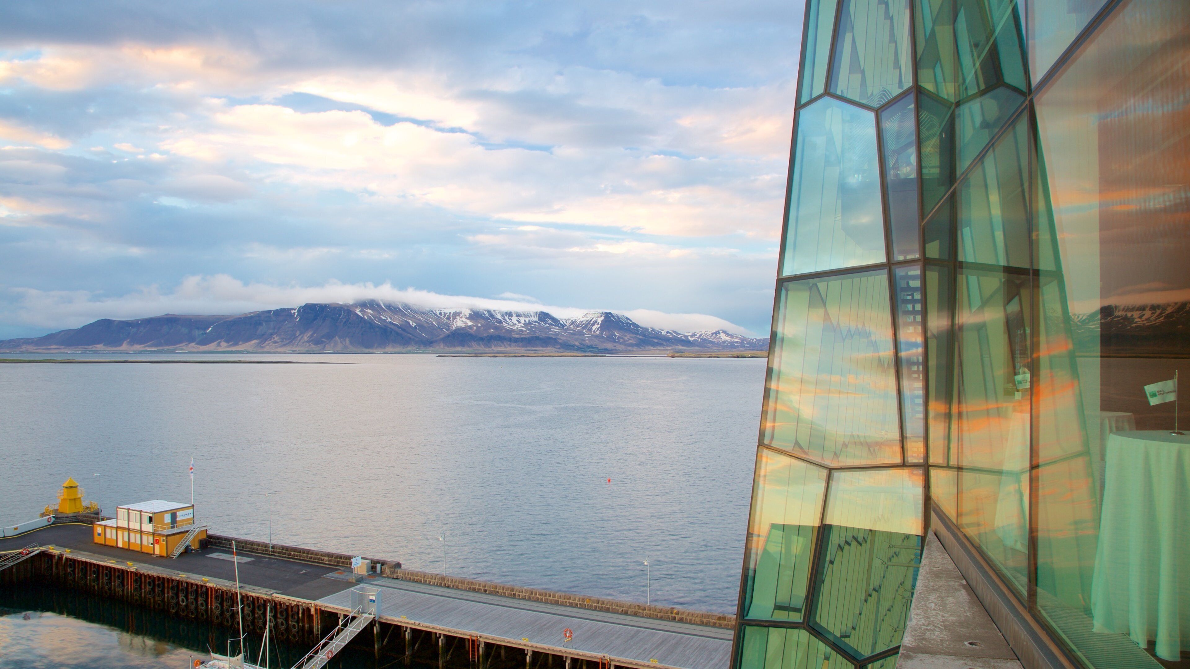 Um edifício de vidro moderno com vista para um lago calmo e montanhas nevadas ao longe.
