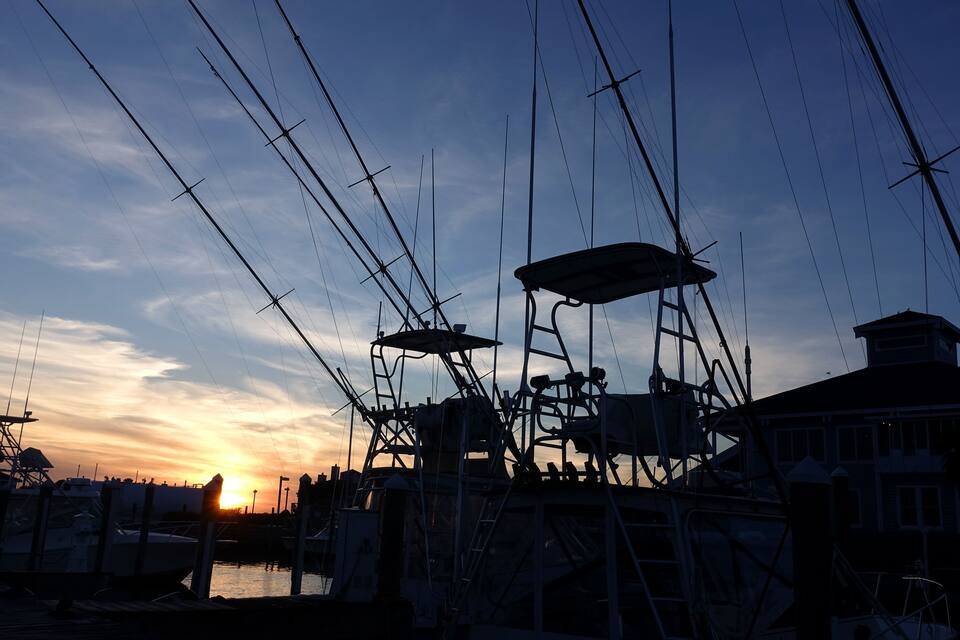 Uma marina ao pôr do sol, com vários barcos atracados e mastros em silhueta contra o céu.
