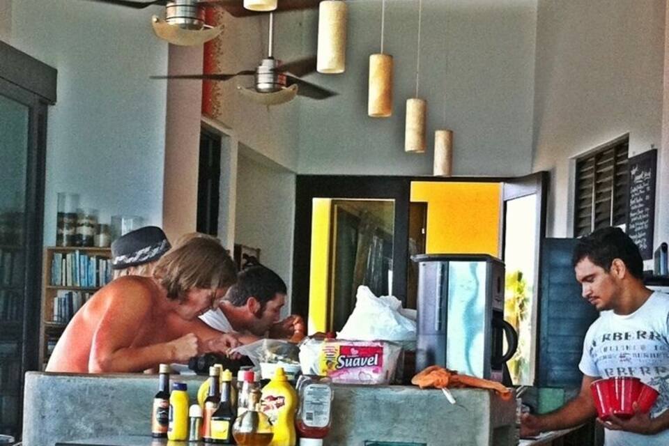 Um bar com luminárias pendentes, um balcão com acompanhamentos e alguém preparando bebidas.