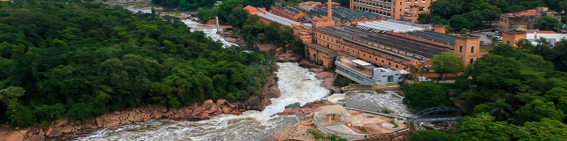 Um rio serpenteando por uma cidade com edifícios industriais e uma ponte.