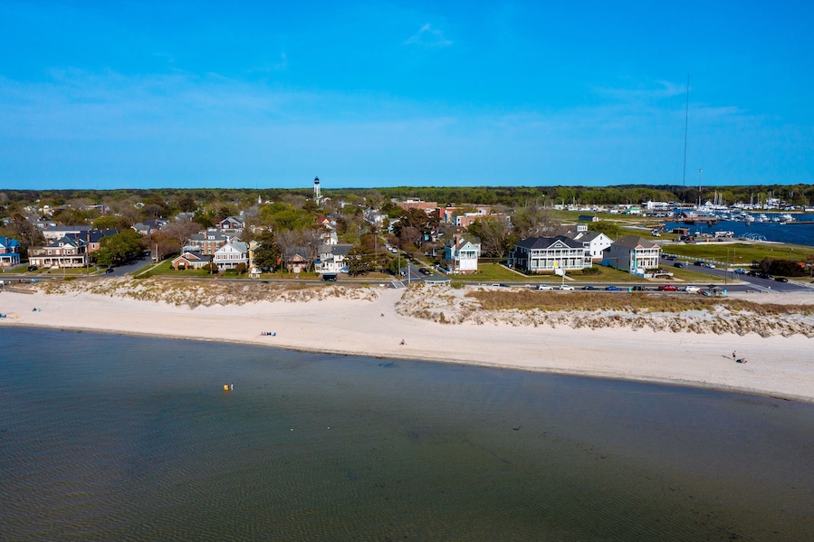 Uma cidade costeira com praia de areia, casas e um farol.
