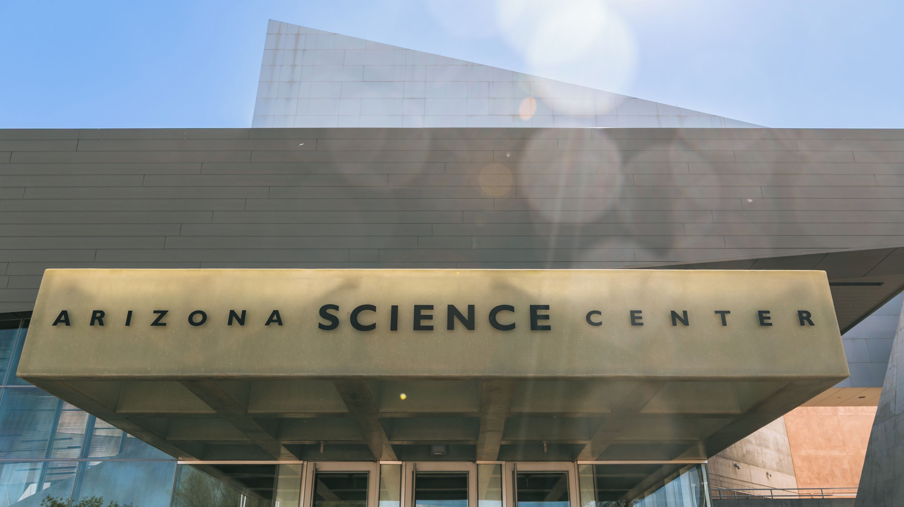 Entrada do Arizona Science Center, com fachada de vidro moderna e uma placa acima das portas.