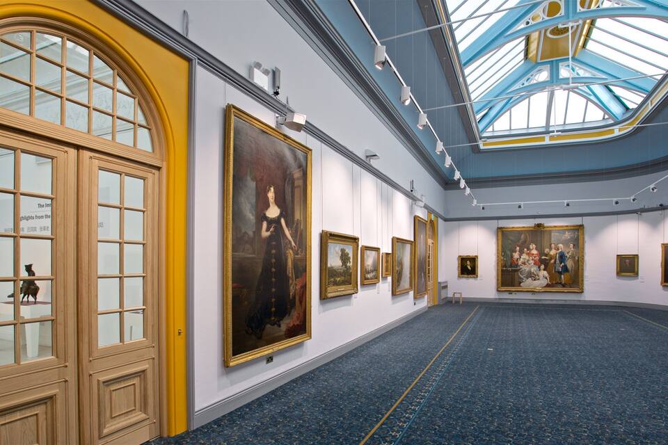 Uma galeria de arte com grandes pinturas nas paredes e uma claraboia acima.