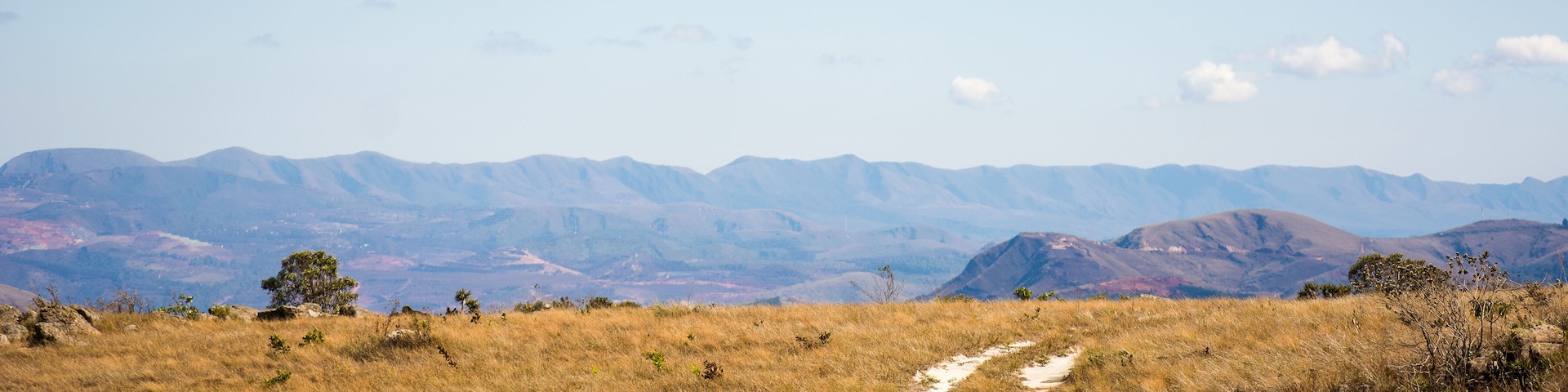 Uma pradaria seca com uma trilha de terra que leva em direção a montanhas distantes sob um céu claro.