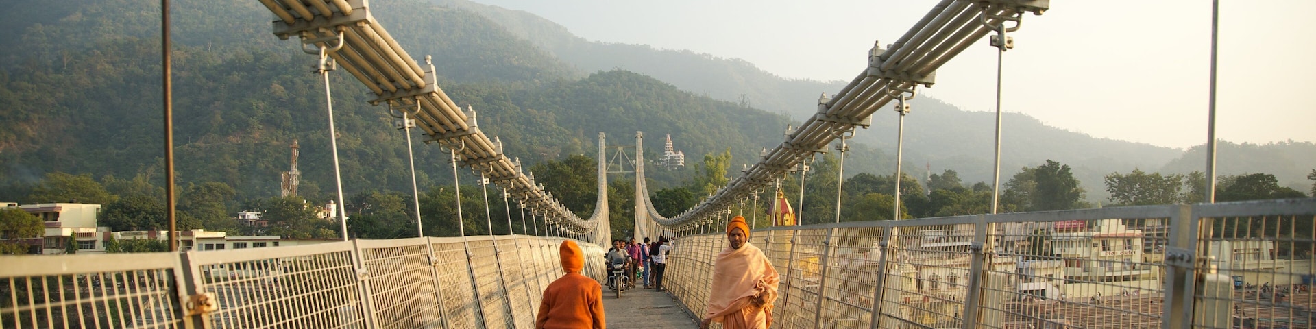 Ram Jhula mostrando uma ponte suspensa ou passarela entre as árvores e uma cidade pequena ou vila assim como um pequeno grupo de pessoas