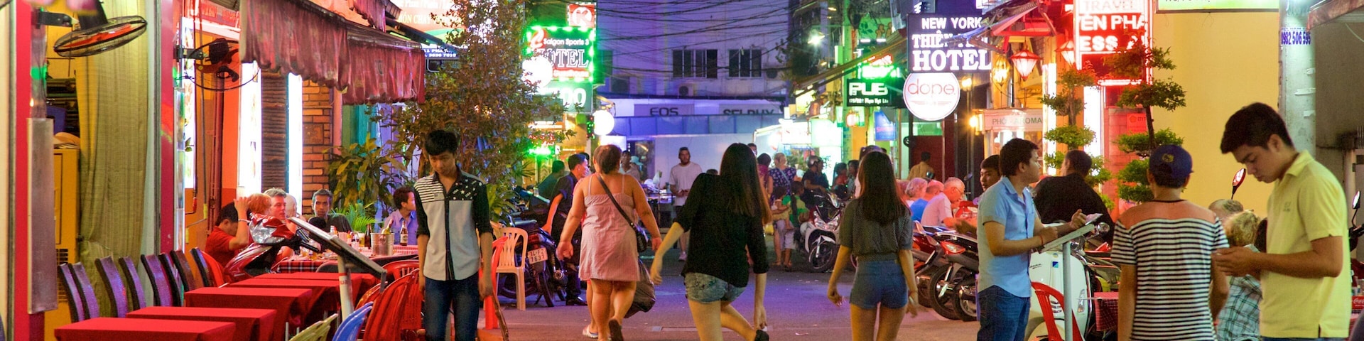 Rua movimentada com letreiros de neon, motocicletas e pessoas caminhando.