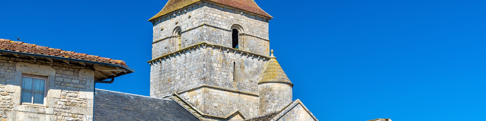 Uma igreja de pedra histórica, com torre sineira e janelas em arco.