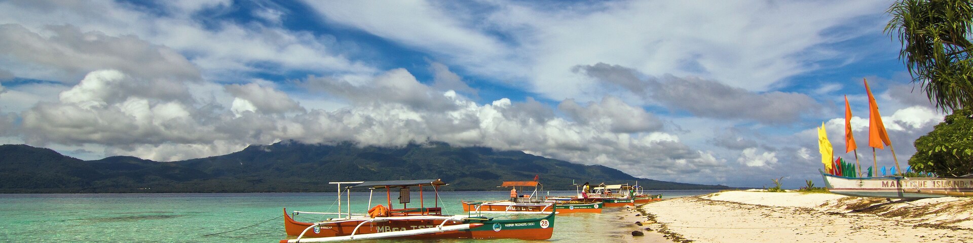 Uma praia com águas turquesa cristalinas, barcos e uma cordilheira ao fundo.
