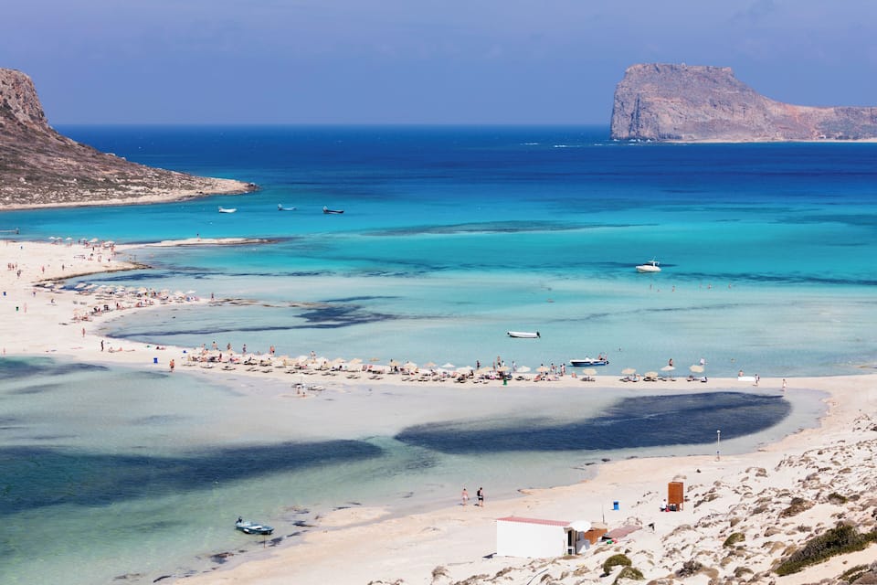 Uma praia costeira com águas turquesa cristalinas, areal arenoso e falésias rochosas.