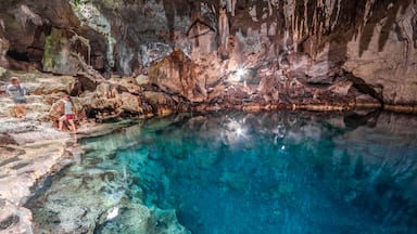 Uma caverna com água cristalina, formações rochosas e pessoas explorando.
