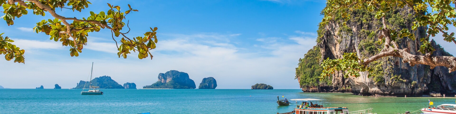 Uma praia com barcos, água cristalina e uma grande formação rochosa.
