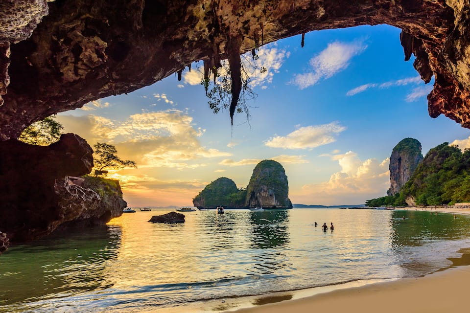 Cena costeira com uma abertura de caverna, água cristalina e uma ilha distante com um barco.