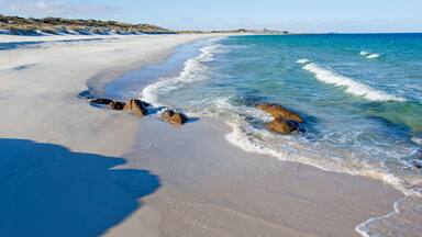 Uma praia de areia com águas azul-claras, rochas e dunas.