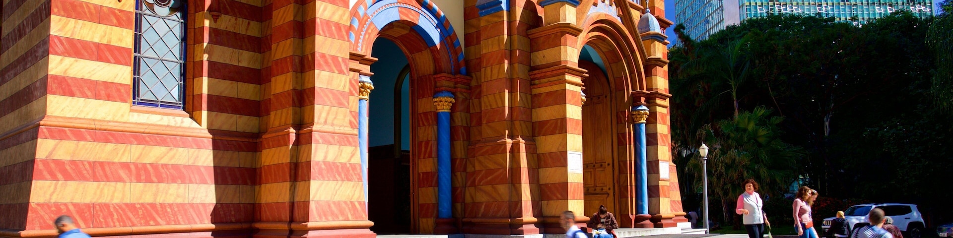 Um edifício histórico com paredes listradas em vermelho e amarelo, grandes portais em arco e uma escadaria que leva à entrada.
