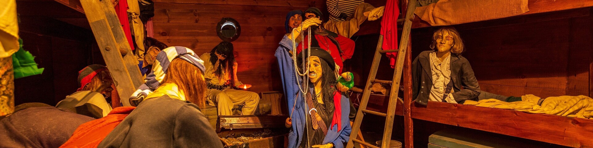 Interior de uma cabana de madeira com beliches, escada e diversos objetos pessoais.