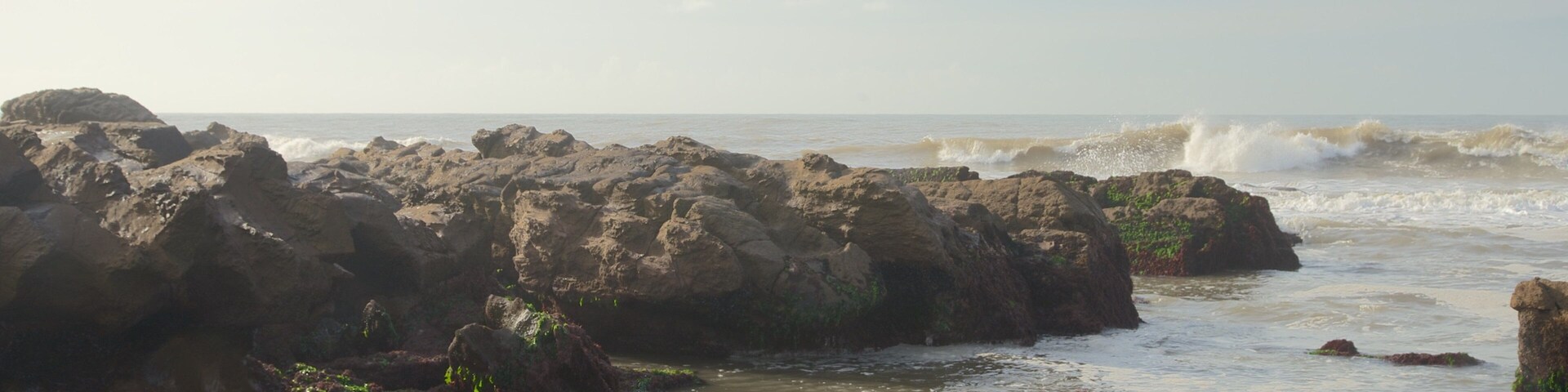 Litoral rochoso com ondas quebrando nas pedras.