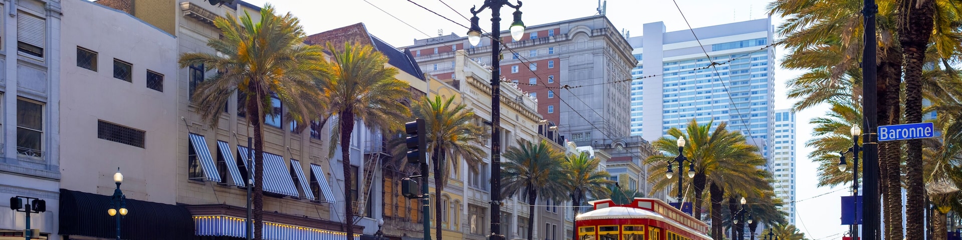 Rua com bondinho vermelho, palmeiras e edifícios com toldos listrados.