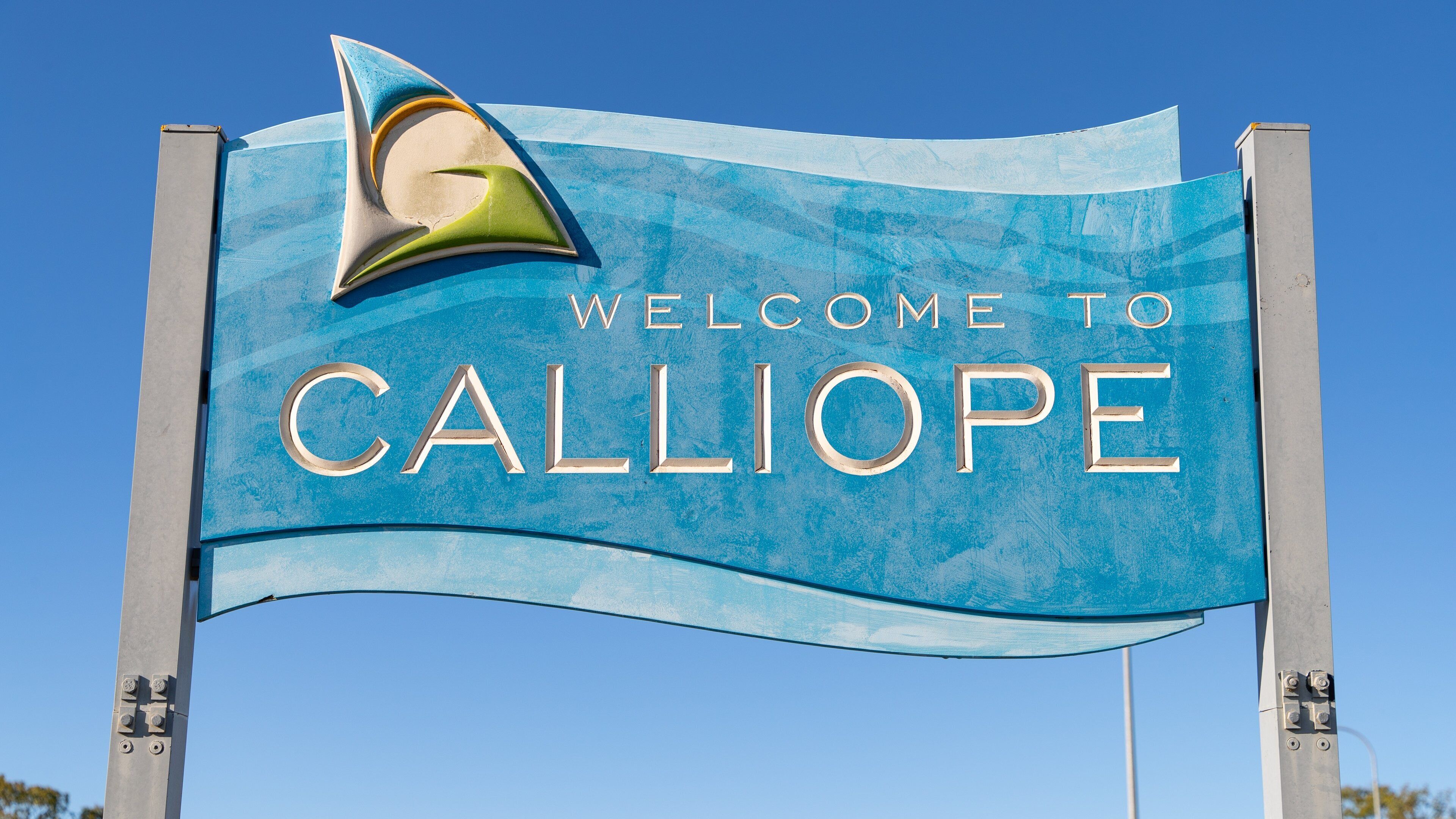 Uma placa de boas-vindas azul com o texto 'WELCOME TO CALLIOPE' e um logotipo estilizado em forma de 'G'.