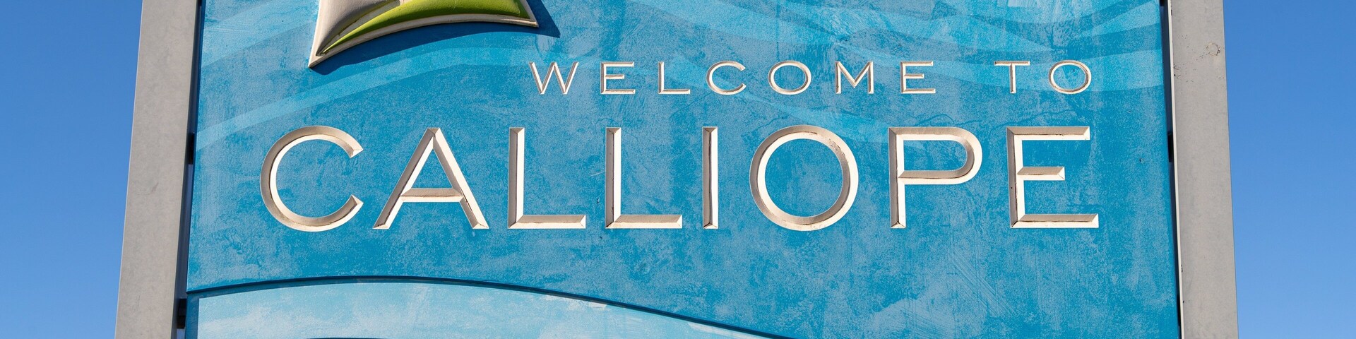 Uma placa de boas-vindas azul com o texto 'WELCOME TO CALLIOPE' e um logotipo estilizado em forma de 'G'.