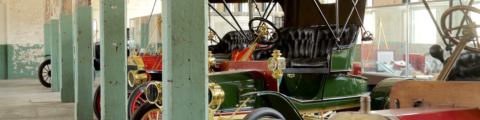 Uma exposição de carros antigos com vários veículos clássicos exibidos sob um teto alto com vigas aparentes.