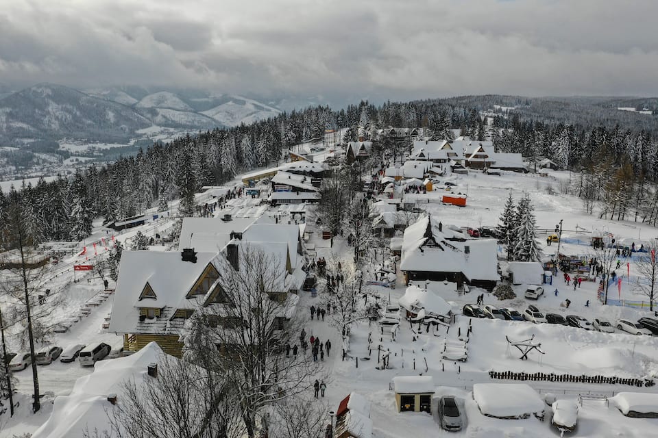 Estância de esqui coberta de neve, com edifícios, árvores e montanhas ao fundo.
