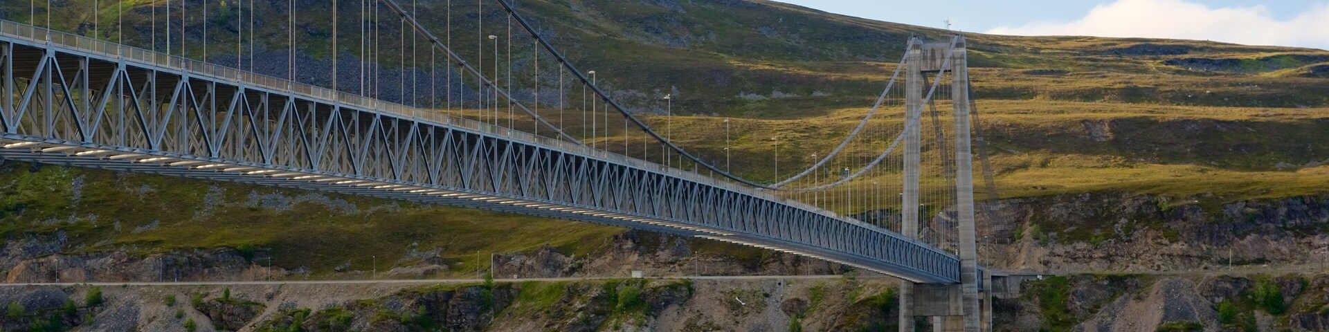 Uma ponte suspensa sobre a água, com uma paisagem montanhosa ao fundo.