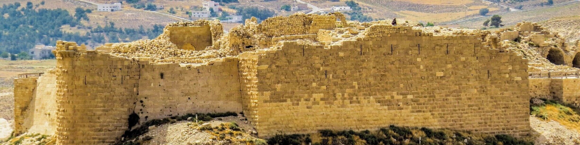 Uma fortaleza de pedra histórica com ruínas e uma paisagem acidentada ao fundo.