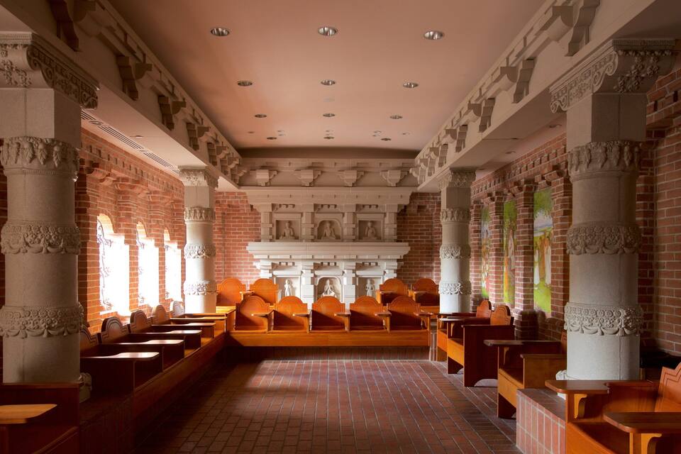 Interior de igreja com paredes de tijolo, bancos de madeira e colunas elaboradas.