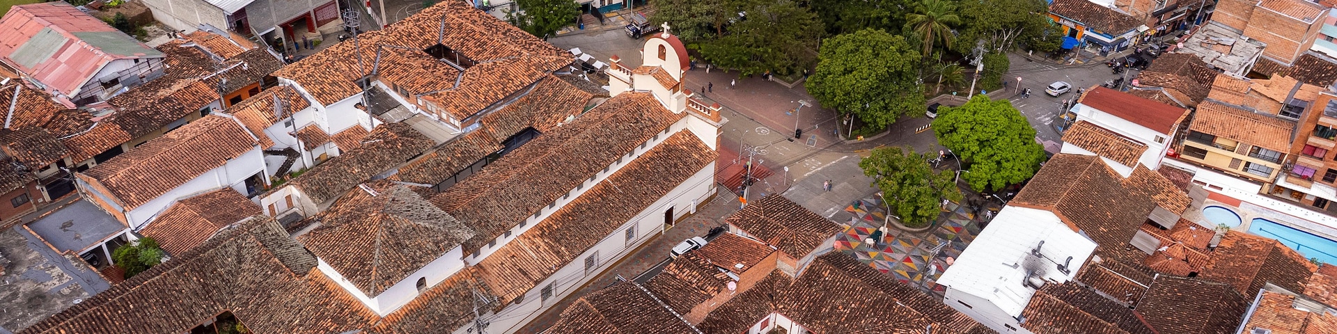 Vista aérea de uma área urbana densamente construída, com telhados de ladrilho vermelho, uma igreja imponente com uma torre sineira e uma mistura de edifícios residenciais e comerciais.