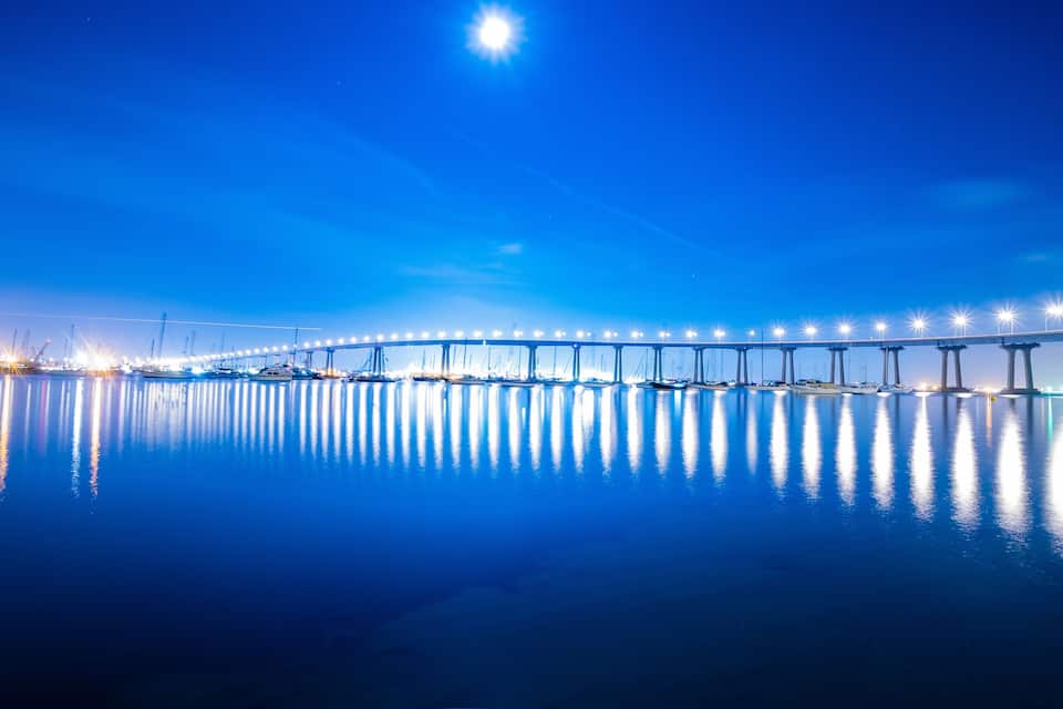 Uma ponte à noite, com suas luzes refletindo na água.