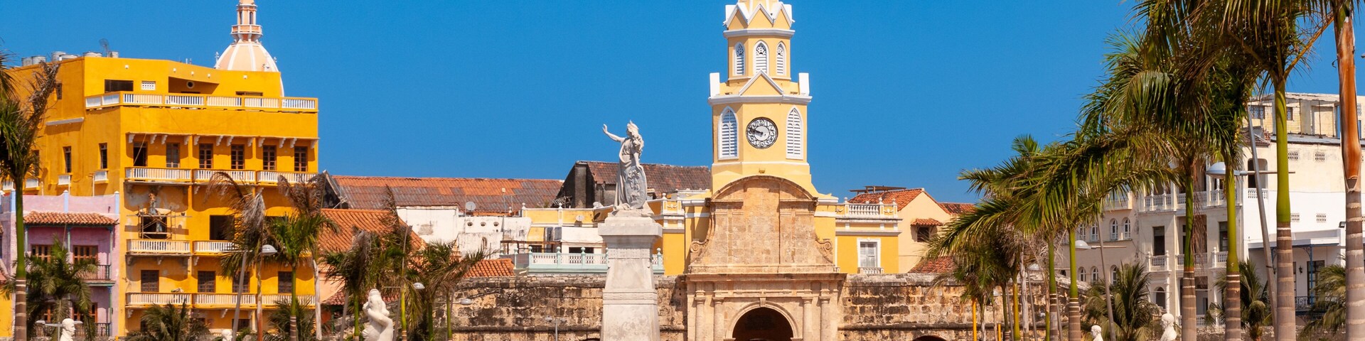 Uma praça com uma torre do relógio, uma estátua e uma fonte.