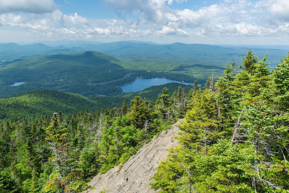 Paisagem montanhosa com florestas densas, uma estrada sinuosa e um lago.