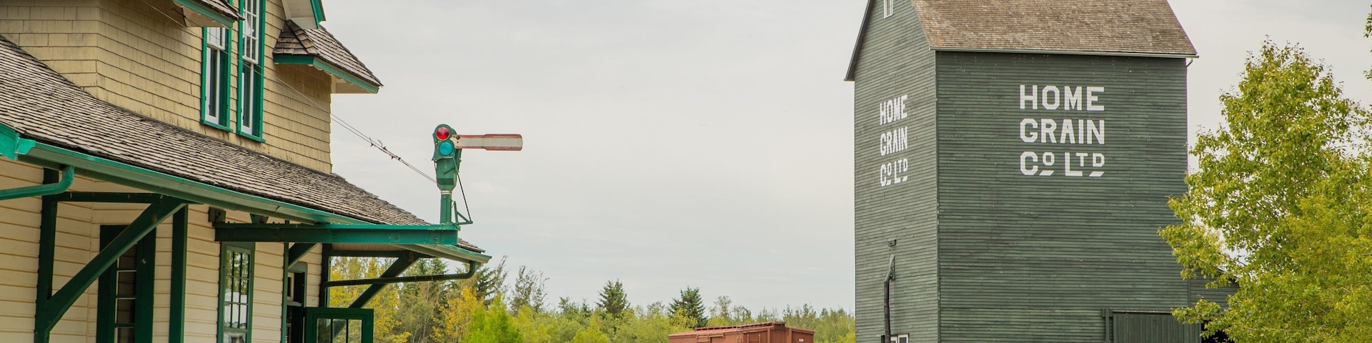 A historic train station with a green grain silo labeled "HOME GRAIN CO. LTD."