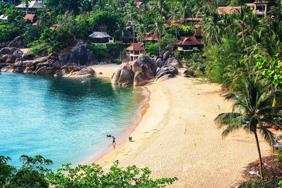 Uma praia tropical com águas cristalinas turquesa, pedras grandes e palmeiras.