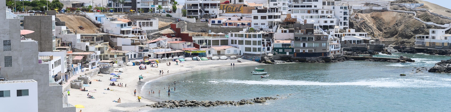 Uma vila costeira com uma praia, edifícios e uma colina ao fundo.