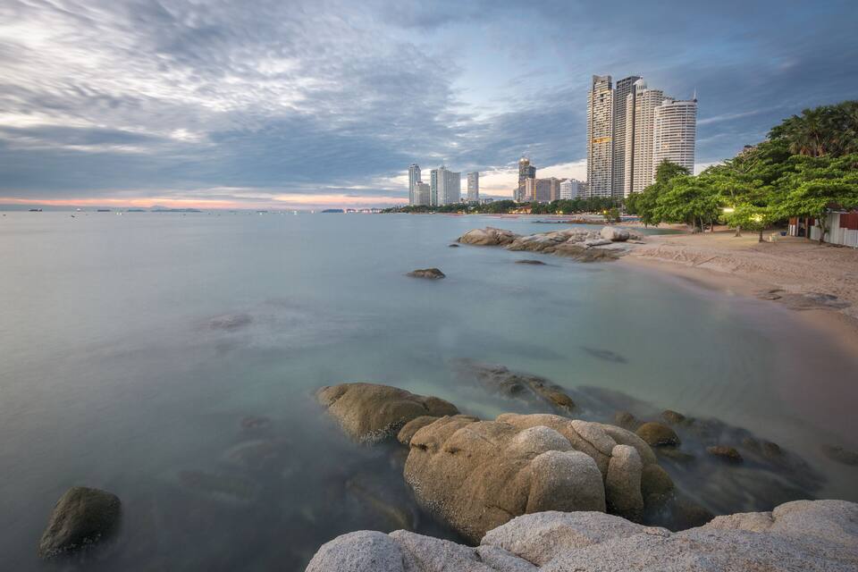 Paisagem costeira urbana com uma praia, costa rochosa e edifícios altos sob um céu nublado.