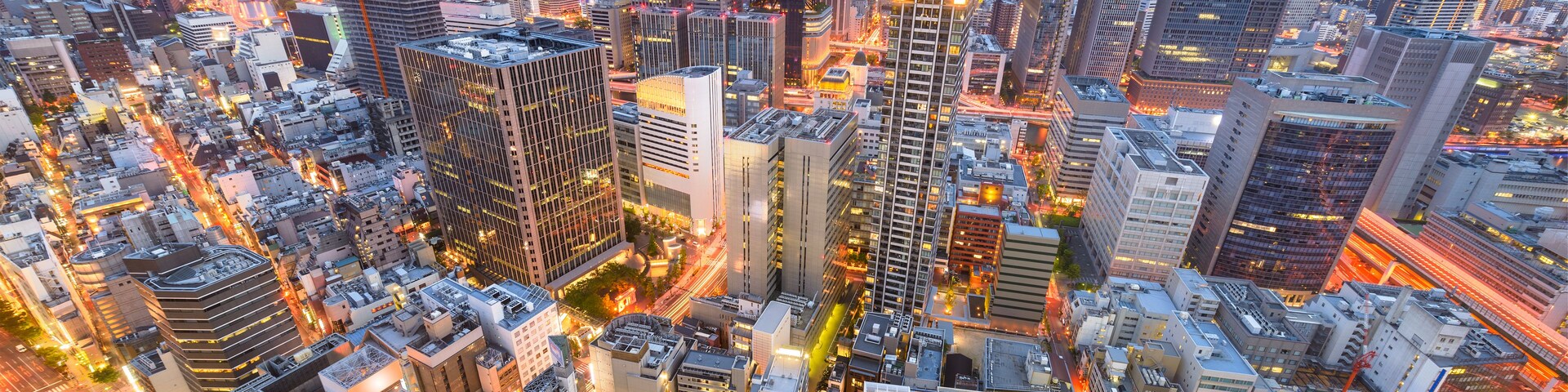Paisagem urbana ao entardecer, com edifícios iluminados e rua movimentada.