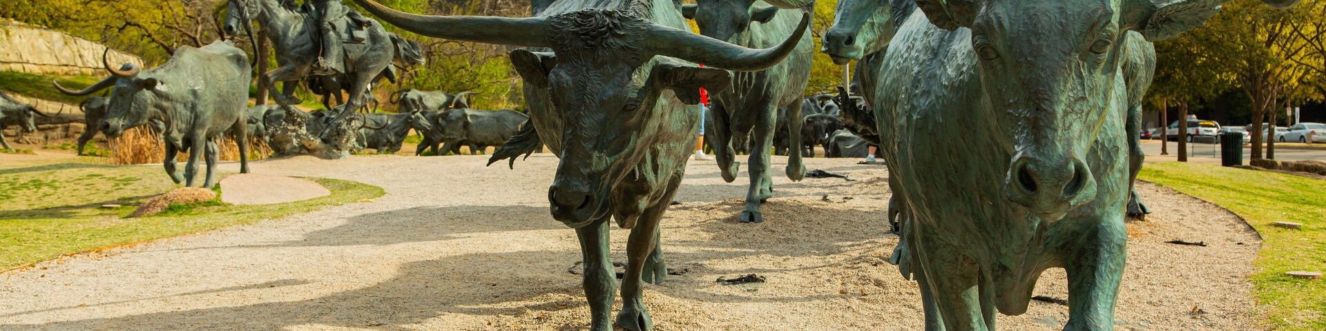Várias esculturas de bronze retratam bois e uma estátua de um cowboy em um caminho de cascalho.