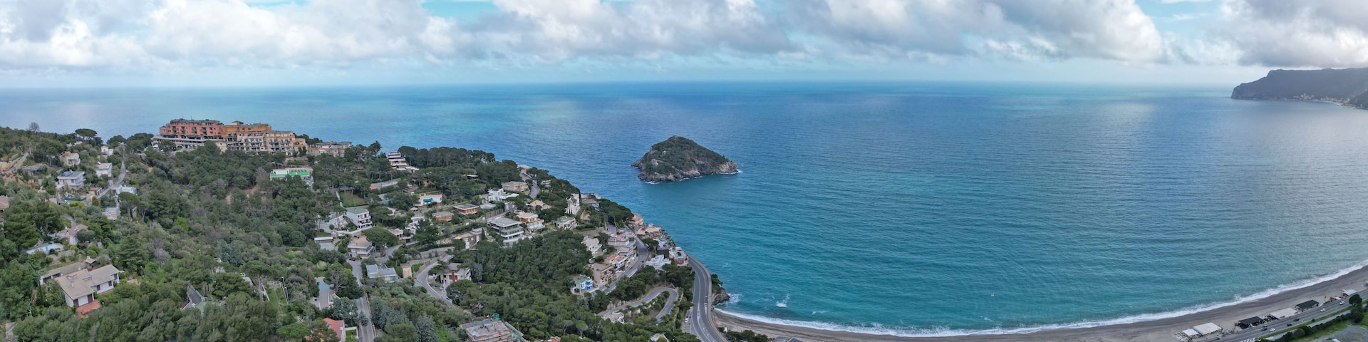 Uma vila costeira com uma estrada sinuosa, uma pequena ilha e um mar azul transparente.