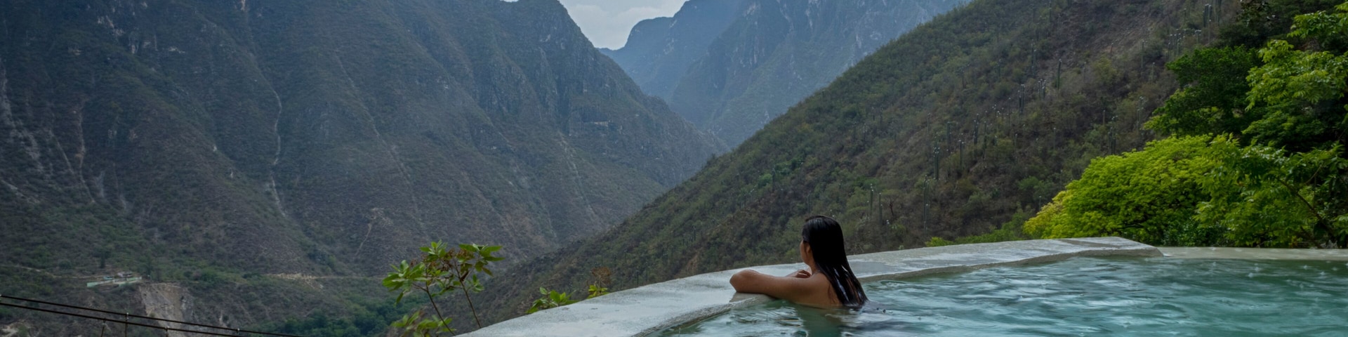 Uma pessoa em uma piscina infinita com vista para uma paisagem montanhosa.